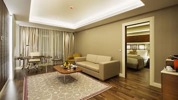 Quarto de hotel com sofá, mesa de jantar, mesinha de centro, cama e banheiro visível por uma porta aberta.