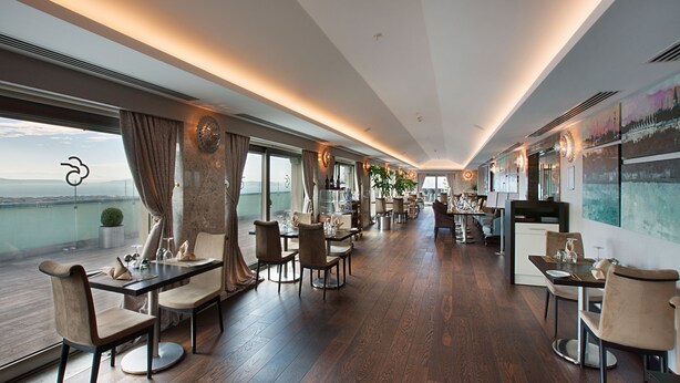 Uma sala de jantar ampla, com mesas e cadeiras altas, janelas grandes com vista para o mar e design de interiores moderno.
