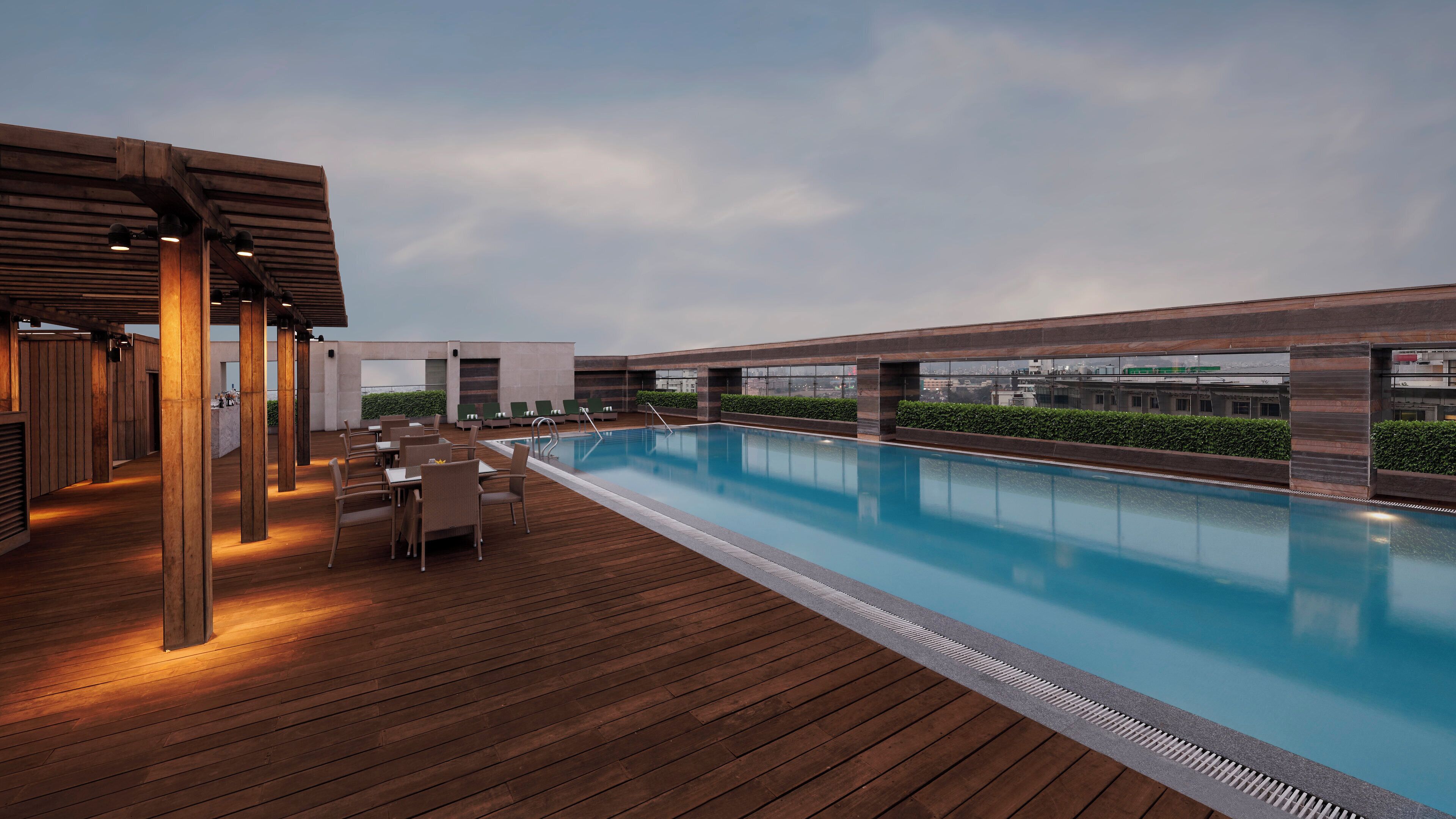 Piscina no terraço com deck de madeira, espreguiçadeiras e mesas.
