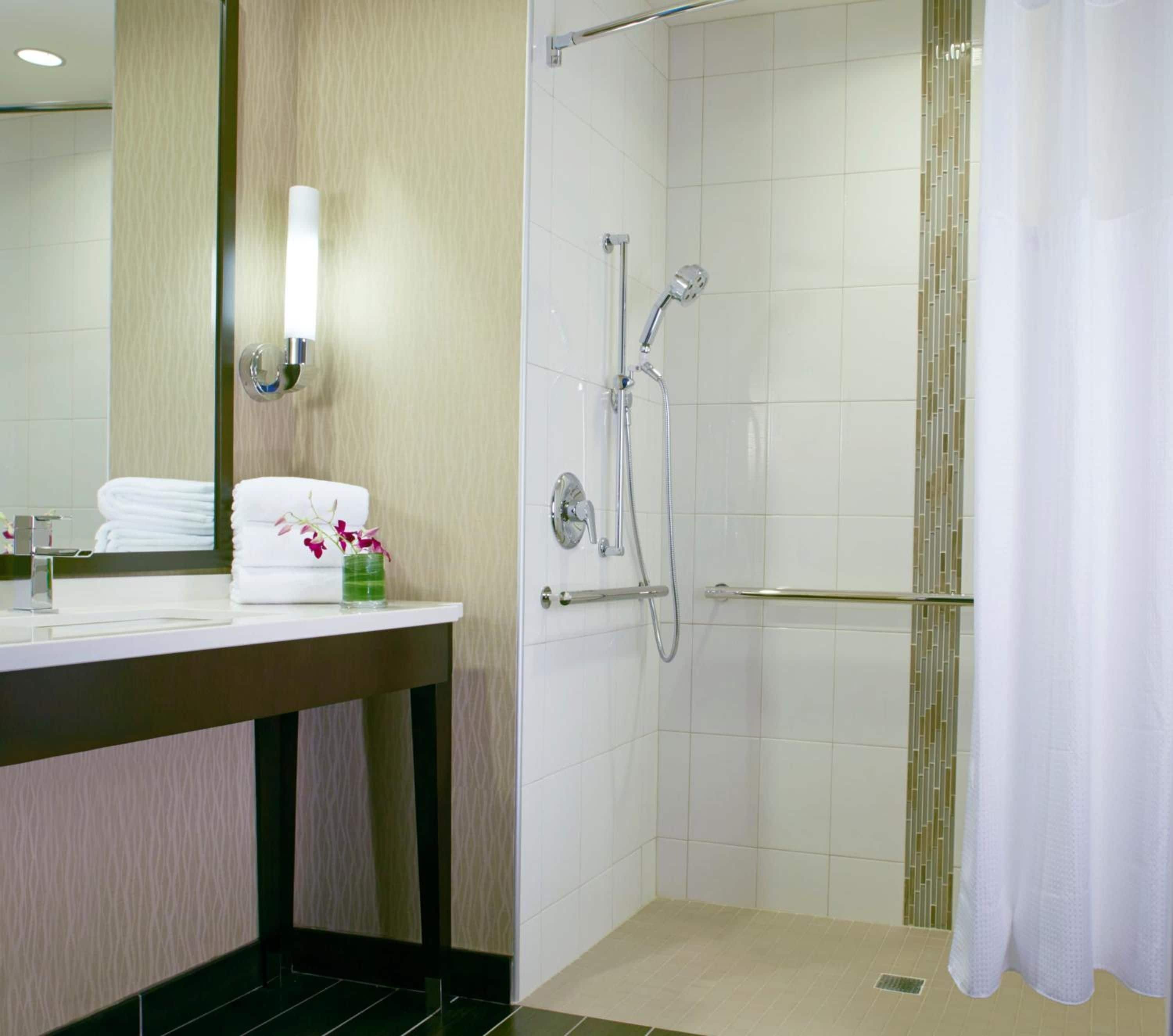 Casa de banho moderna com chuveiro, lavatório com espelho e porta-toalhas.