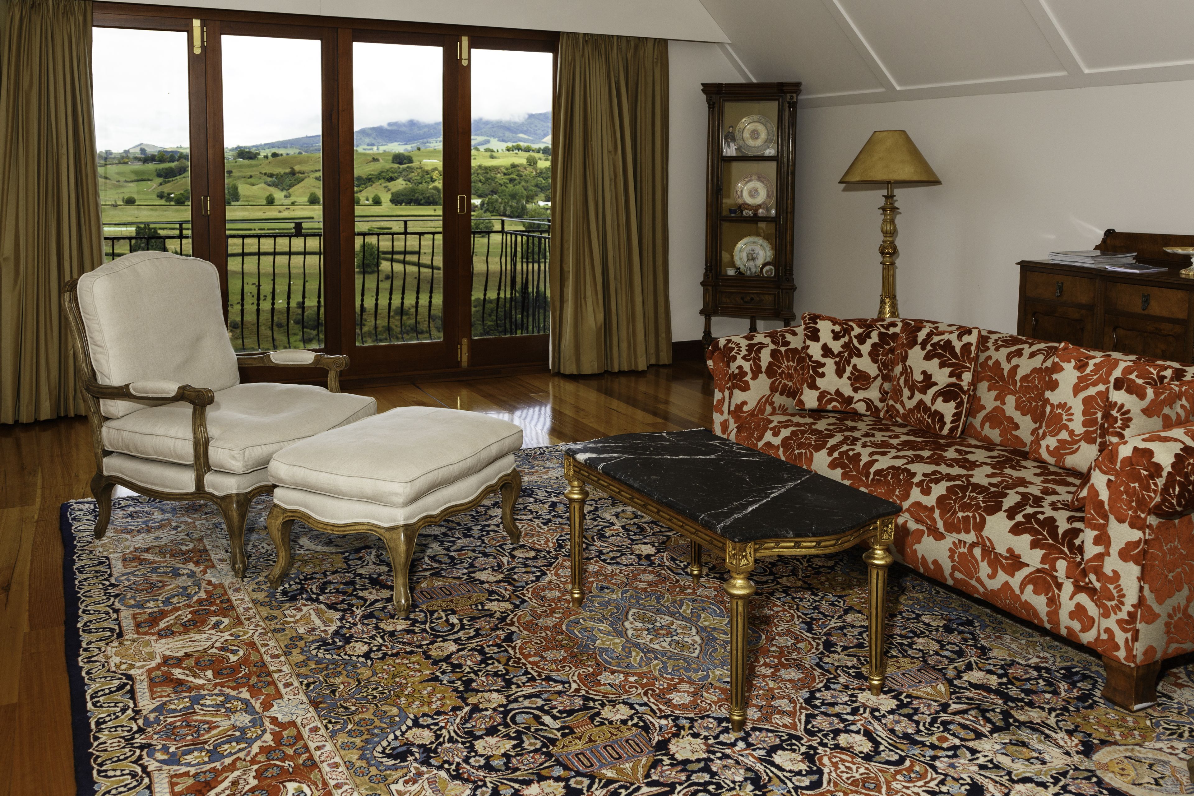Um quarto com uma janela grande, um sofá, uma cadeira, uma mesa e um abajur.