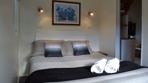 Quarto de hotel com cama, almofadas, um quadro e duas luminárias de parede.