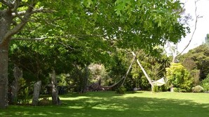 Um jardim exuberante com uma rede, árvores e um gramado bem cuidado.