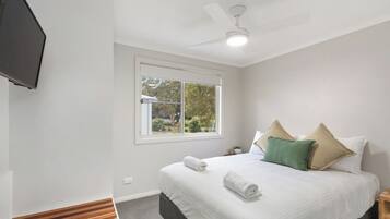 Quarto com cama, janela, ventilador de teto e televisão fixada na parede.