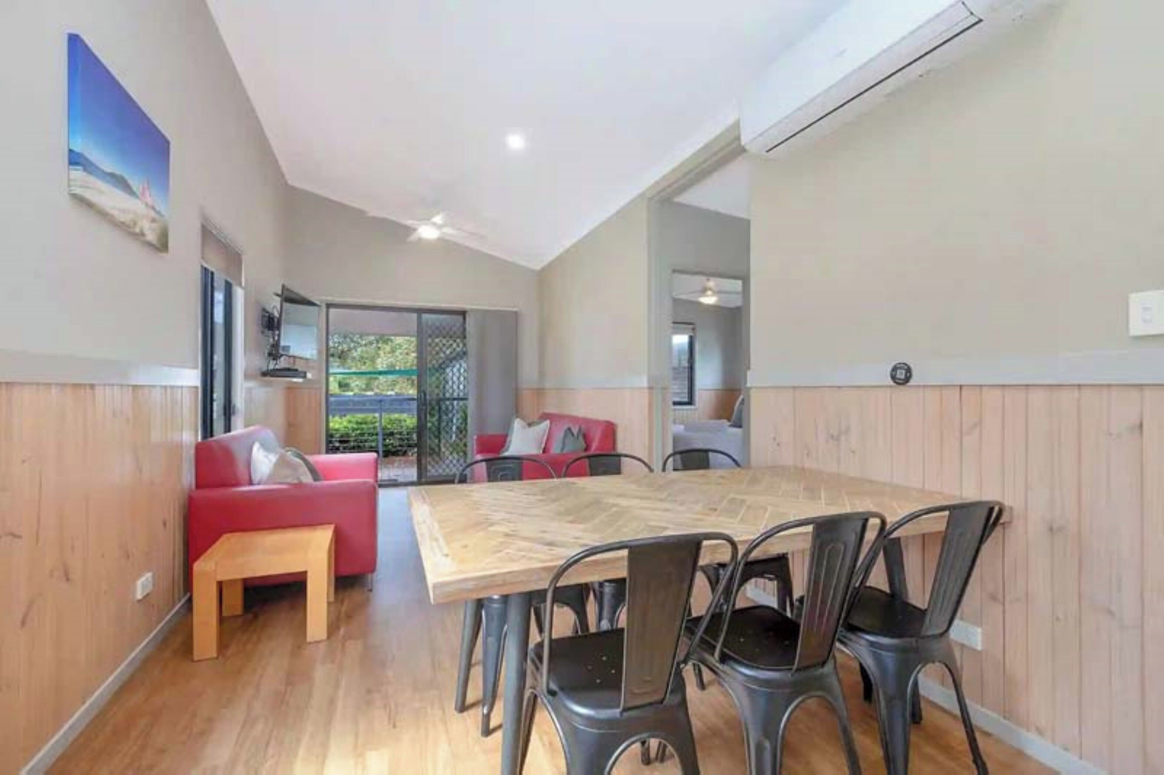 Uma sala de jantar com mesa de madeira e cadeiras de metal, um sofá vermelho e um pequeno banco de madeira.