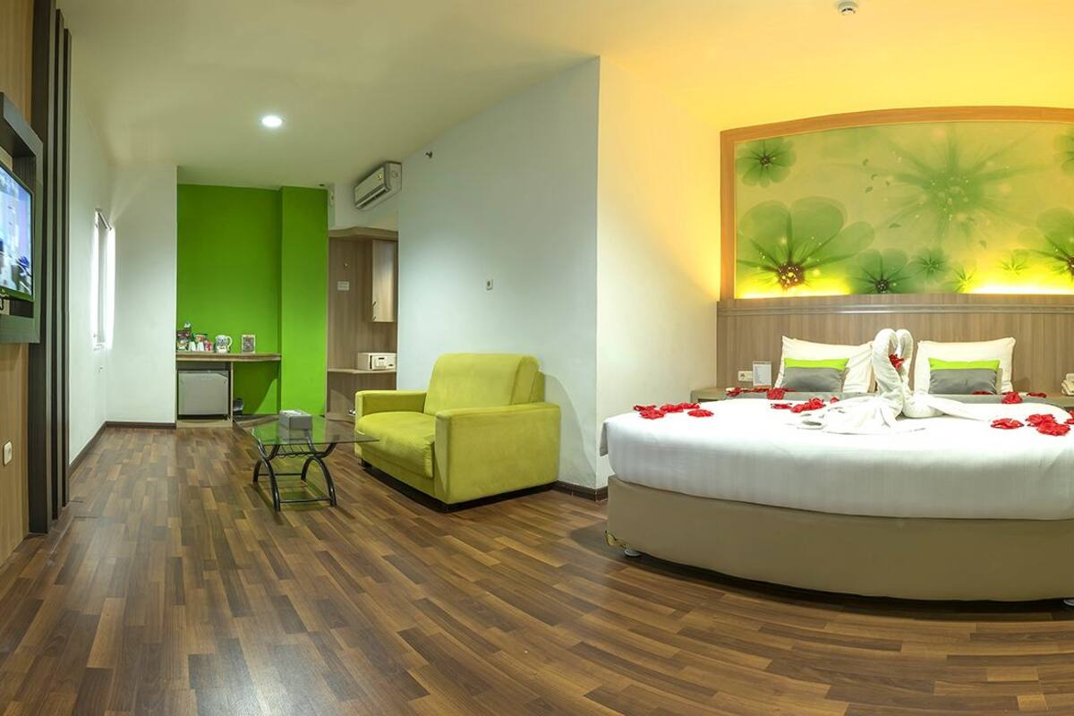 Quarto de hotel com cama, poltrona verde, televisão e parede verde.