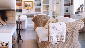 Uma sala de estar aconchegante com lareira, móveis de vime e uma estante de livros ao fundo.