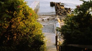 Um cais de madeira que leva a uma costa rochosa, com um mar calmo ao fundo.