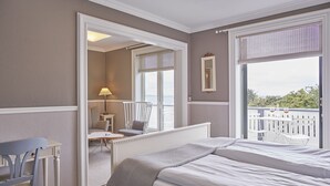 Quarto com cama, poltrona, mesa e janela com vista para o exterior.