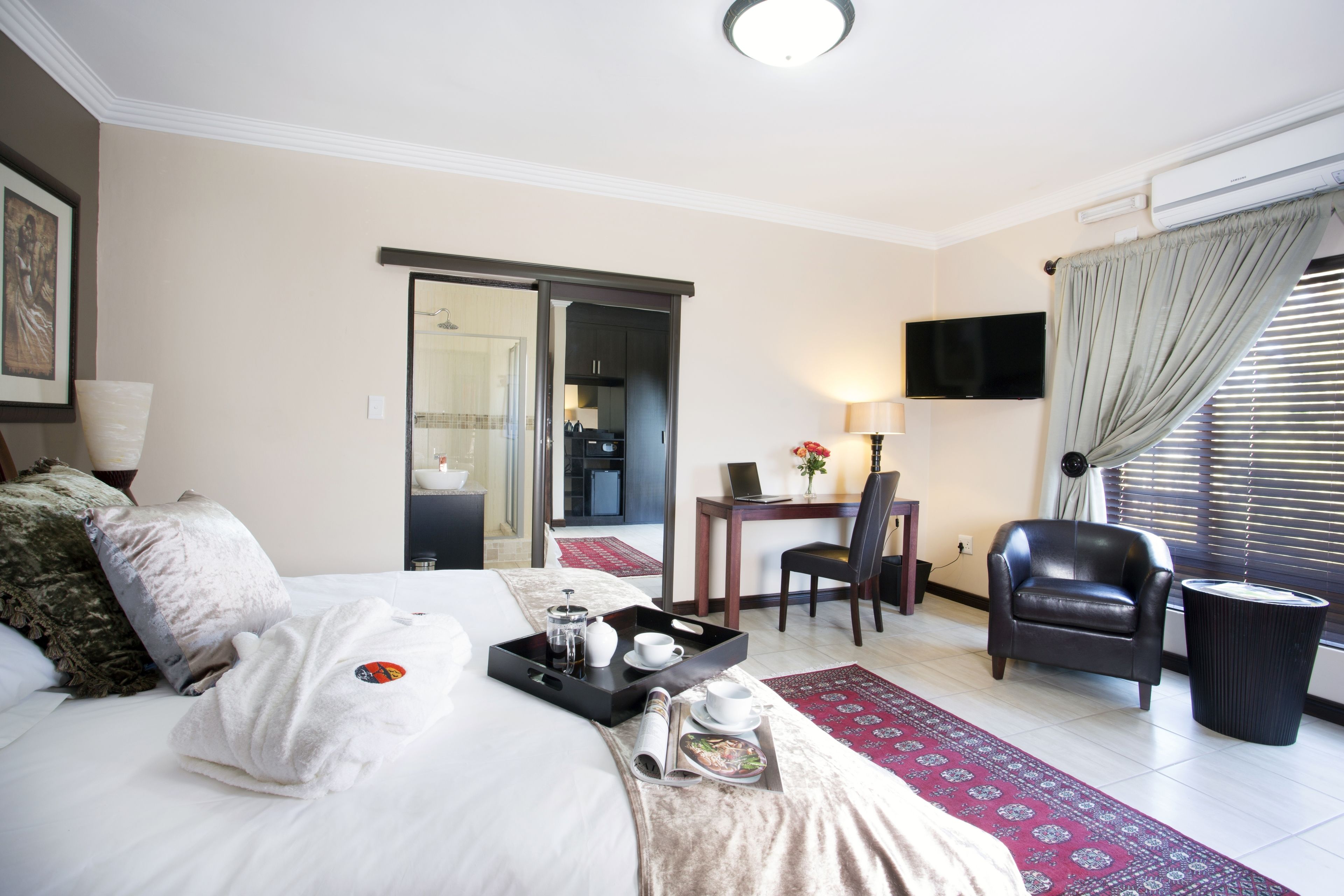Quarto de hotel com cama, escrivaninha com laptop, cadeira, televisão e janela com cortinas.