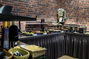 Disposição de buffet com diversos alimentos e parede de tijolos ao fundo.