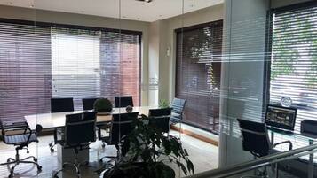 Um espaço de escritório moderno com divisória de vidro, uma mesa de conferência com cadeiras e plantas em vasos.