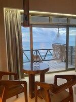 Mesa e cadeiras de madeira num quarto com uma janela ampla com vista para o mar.