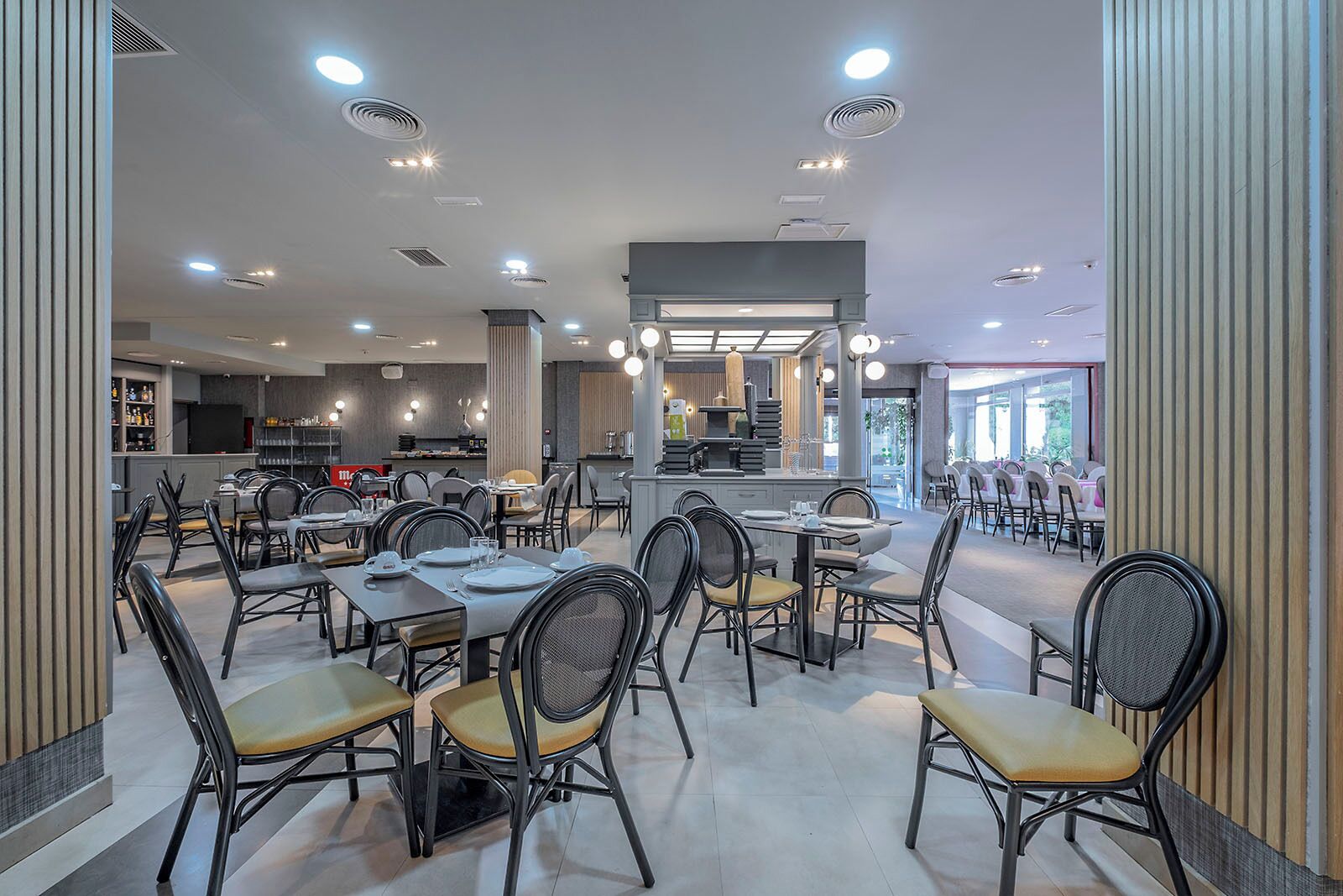Uma ampla área de jantar com várias mesas e cadeiras, um espaço de bar e vista para o exterior.