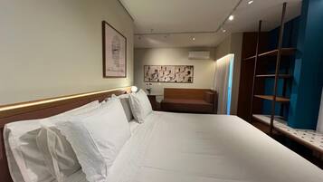 Quarto de hotel com uma cama grande, mesa de cabeceira, uma cadeira e um guarda-roupa.