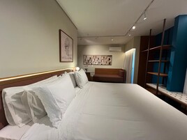 Quarto de hotel com uma cama grande, mesa de cabeceira, uma cadeira e um guarda-roupa.