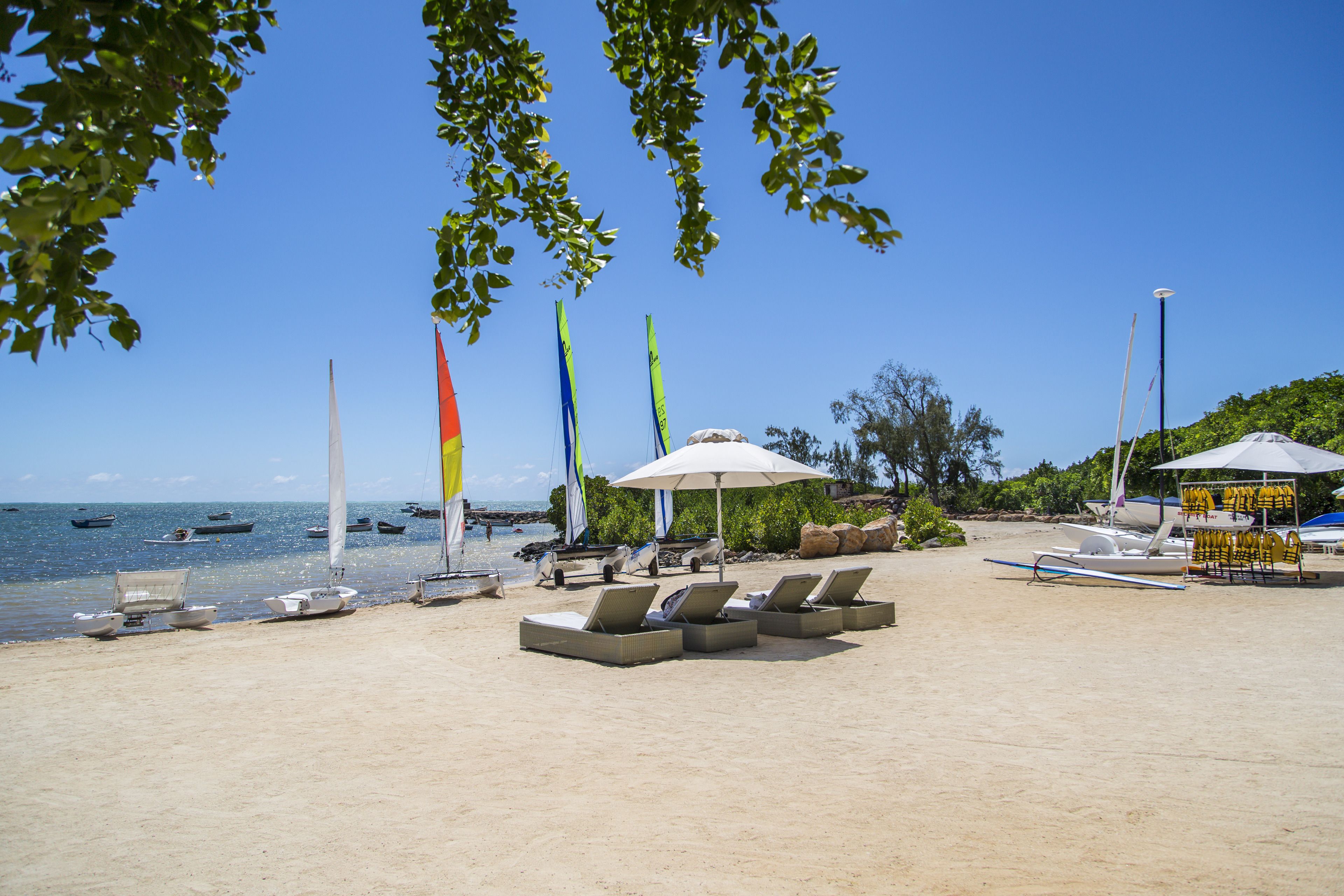Uma praia com cadeiras de praia, guarda-sóis e veleiros.