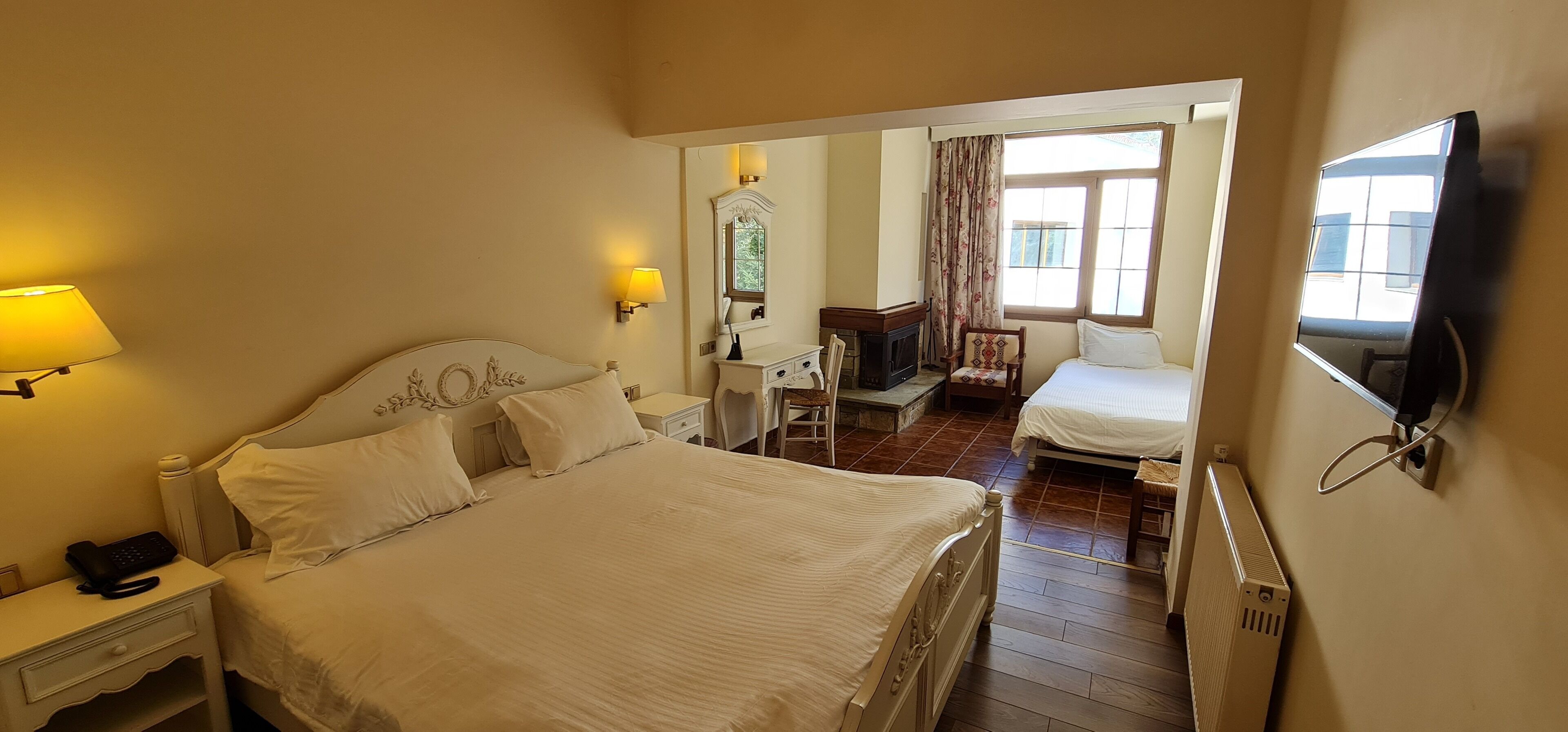 Quarto de hotel com uma cama grande, abajures, televisão, mesa pequena, uma cadeira e lareira.