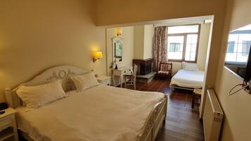 Quarto de hotel com uma cama grande, abajures, televisão, mesa pequena, uma cadeira e lareira.