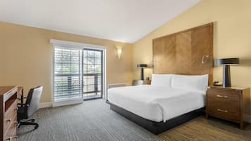 Quarto de hotel com uma cama grande, uma escrivaninha com cadeira, um guarda-roupa, uma mesa de cabeceira com luminárias e uma porta de vidro deslizante para o exterior.
