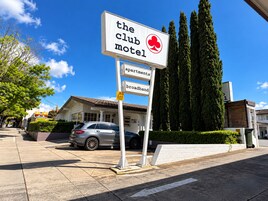 Placa do 'The Club Motel' com símbolo de trevo vermelho, indicando um motel com clube.