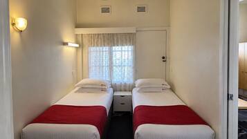 Quarto de hotel com duas camas, um ventilador de teto, uma janela com cortinas e uma porta que dá para uma varanda.