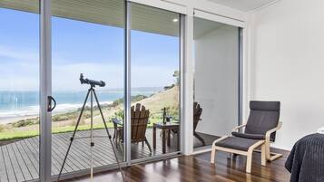 Quarto moderno com uma grande porta de vidro deslizante que dá para uma varanda com um telescópio, cadeiras de madeira e uma mesa.