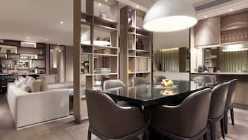Uma sala de jantar moderna com uma mesa de vidro, cadeiras escuras e uma luminária pendente grande.