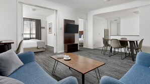 Quarto de hotel com cama, televisão, área de refeições com cadeiras e mesa, e um sofá.