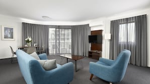 Uma sala de estar moderna com duas poltronas azuis, uma mesa de centro de madeira, uma TV e uma área de jantar com mesa e cadeiras.