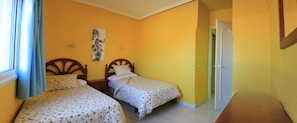 Quarto com duas camas, um quadro na parede e uma porta que dá para outro cômodo.