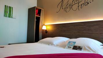 Quarto de hotel com cama, manta vermelha, guarda-roupa, parede com um letreiro e uma lâmpada.