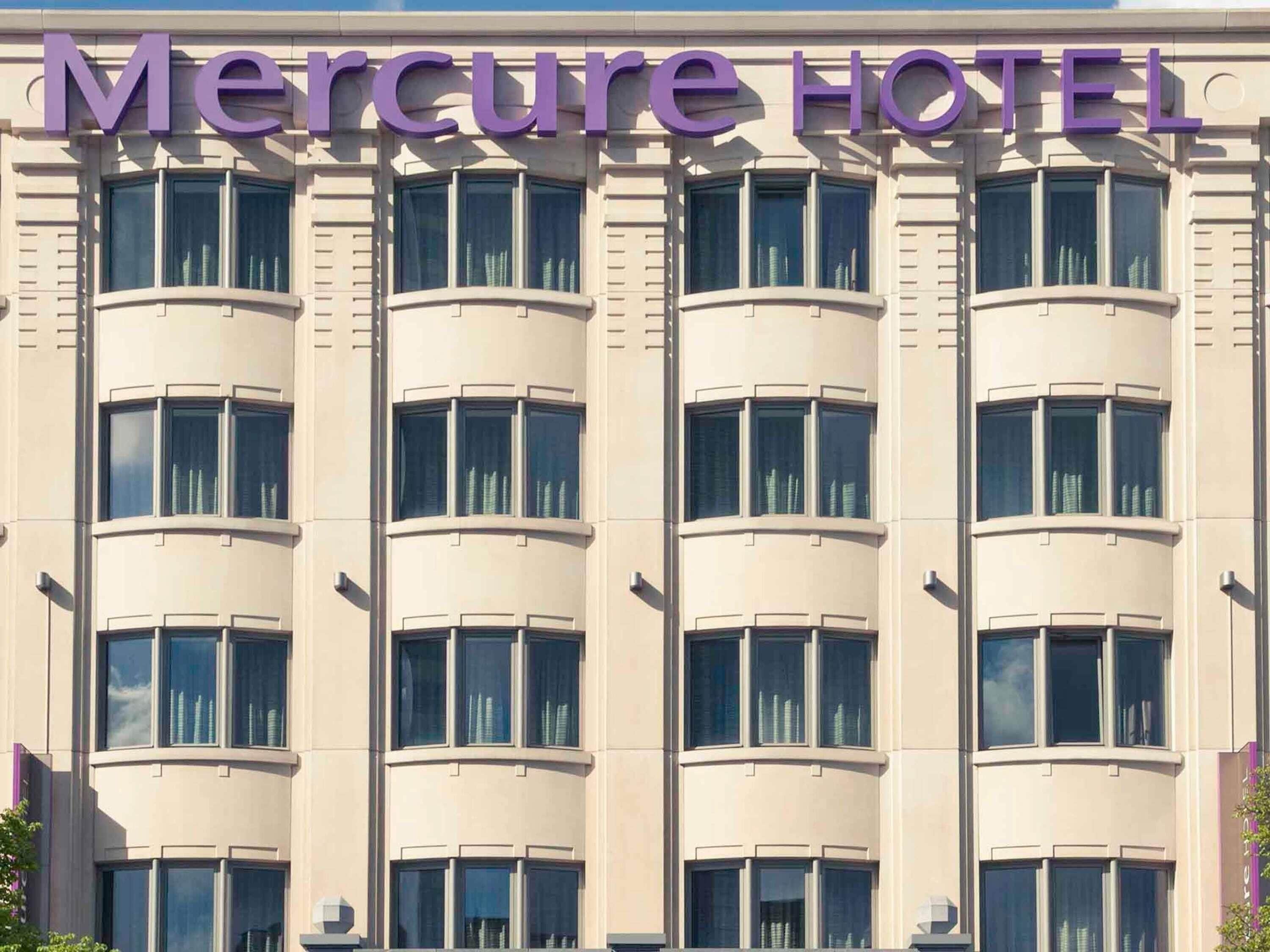 Um edifício de hotel com o nome 'Mercure Hotel' em destaque. Apresenta um estilo arquitetônico moderno, com várias varandas e janelas amplas.