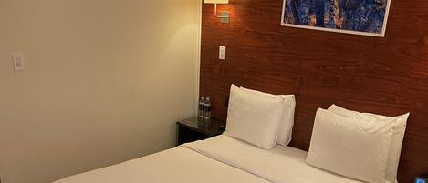 Quarto de hotel com uma cama grande, mesa de cabeceira com abajur e pintura da paisagem urbana na parede.