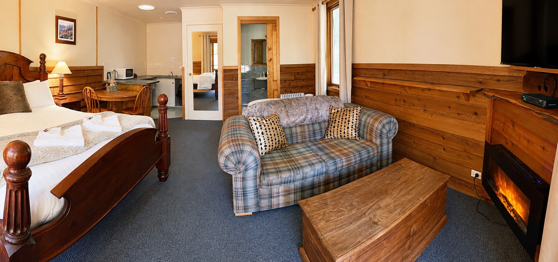 Quarto de hotel com cama, sofá, banco de madeira, televisão, lareira e banheiro visível por uma porta aberta.