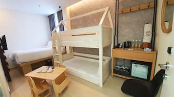 Quarto de hotel pequeno com uma cama beliche, uma escrivaninha de madeira, uma cadeira, uma mesa de cabeceira, uma televisão e um espelho.