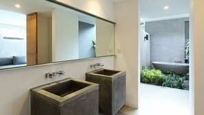 Uma casa de banho moderna com duas grandes pias de pedra, um espelho grande e uma banheira visível ao fundo.