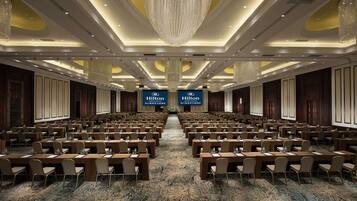 Uma sala de conferências espaçosa com fileiras de mesas e cadeiras, lustres e sinalização Hilton.