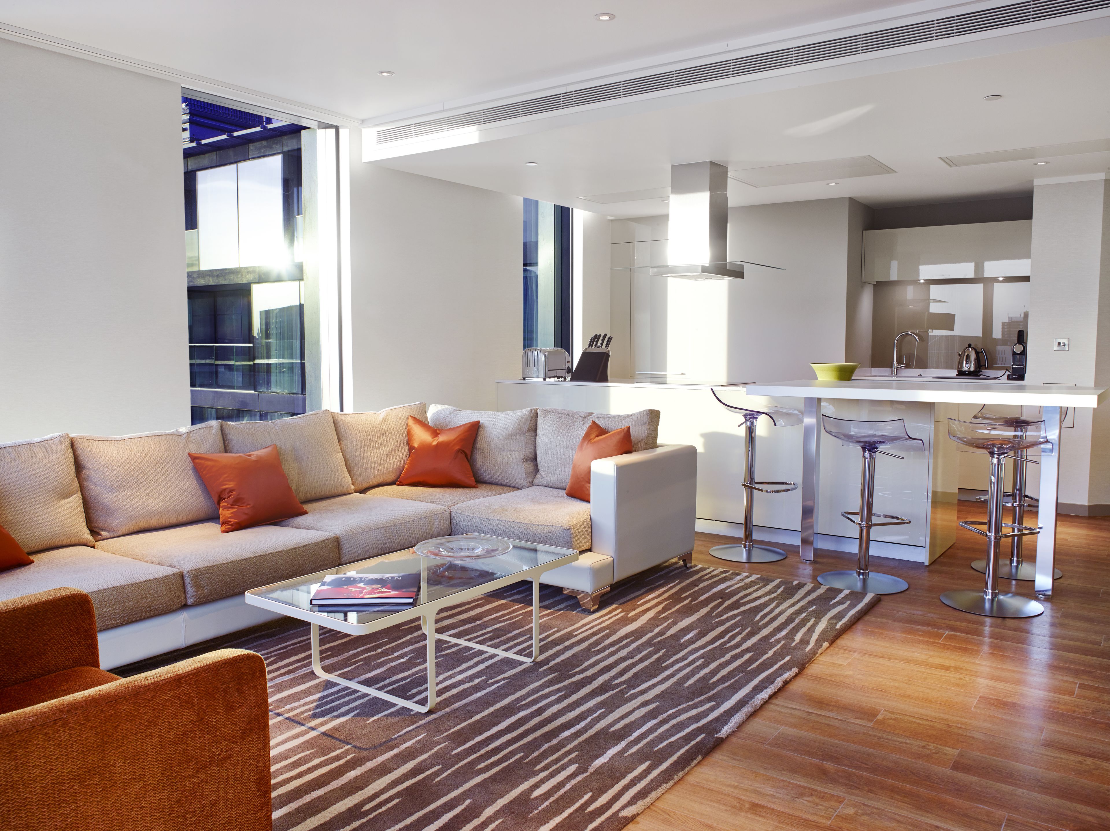 Uma sala de estar moderna com sofá, mesa de centro e mesa de jantar com tampo de vidro e banquetas.