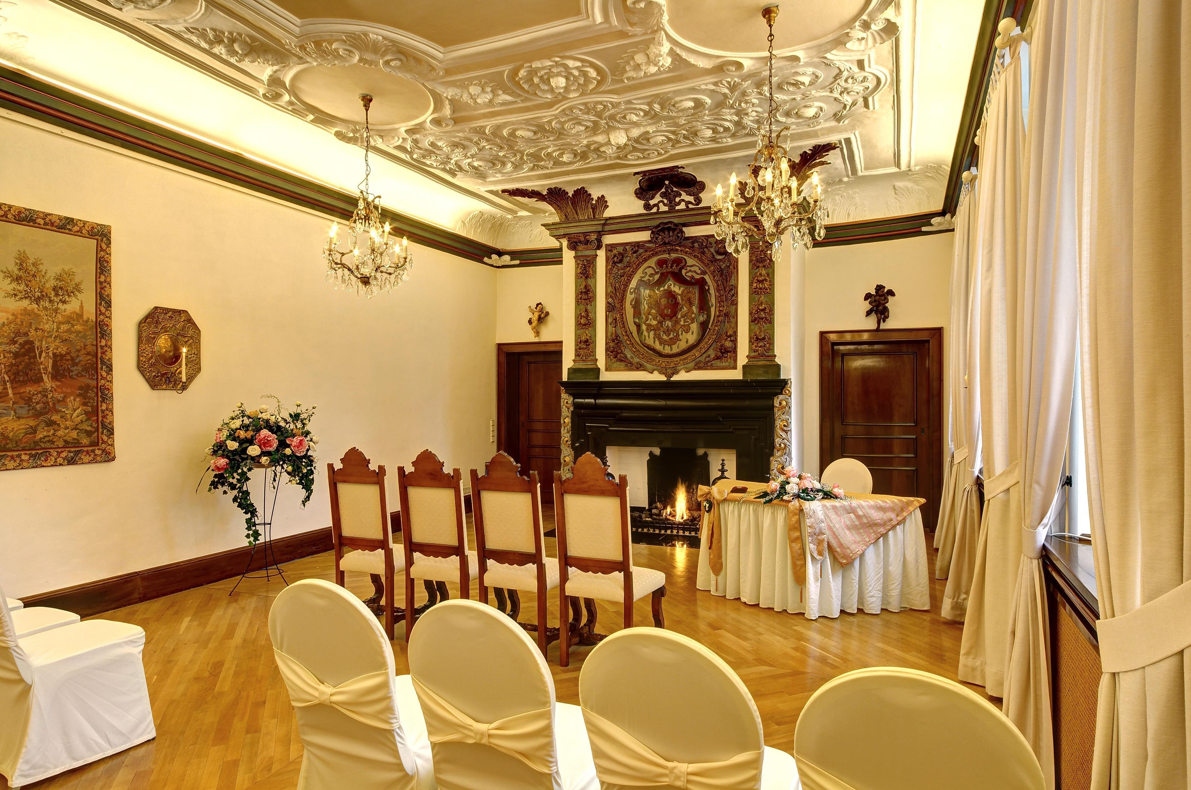 Uma sala de jantar formal com teto ricamente decorado, lustres e lareira.