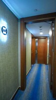 Corredor de hotel com carpete azul, portas de madeira e um aviso na parede.