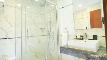 Uma casa de banho moderna com chuveiro de vidro, pia branca e bancada de mármore.
