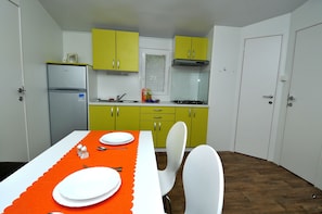 Uma cozinha compacta com uma mesa de jantar posta para dois, apresentando uma toalha de mesa laranja vibrante, pratos brancos e um saleiro e pimenteiro pequenos.