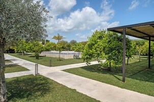 Um jardim ajardinado com um caminho pavimentado, uma pérgola e diversas árvores.