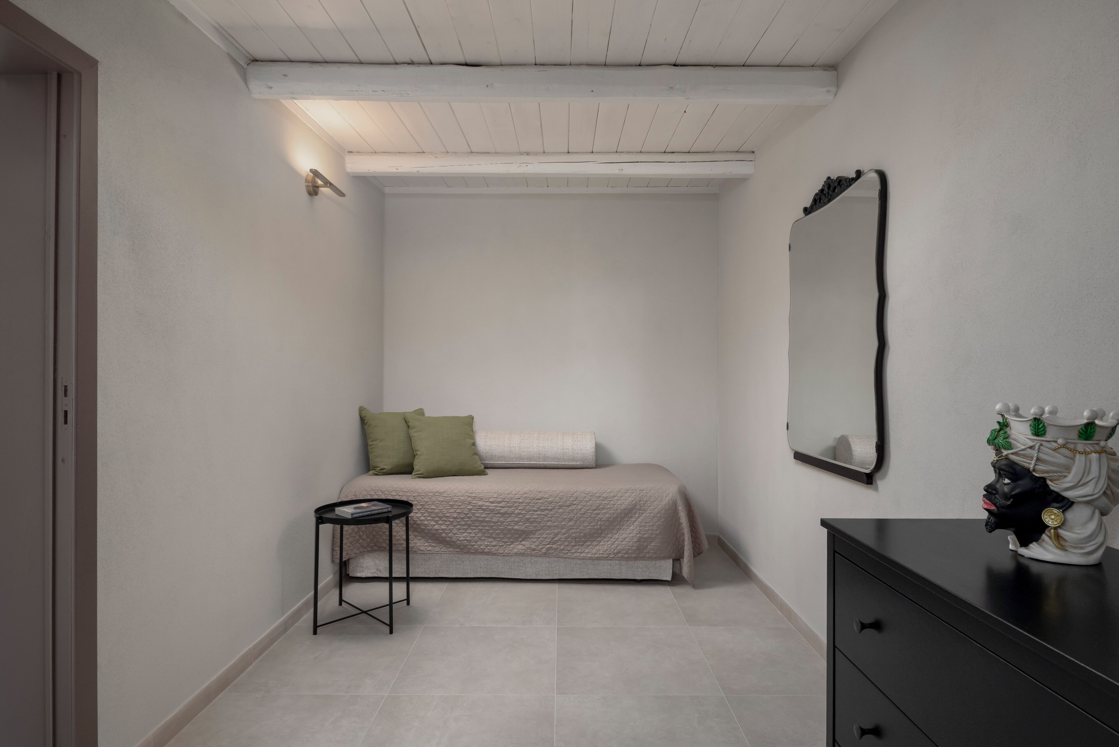 Quarto pequeno e bem organizado, com cama, mesinha, cômoda e espelho.