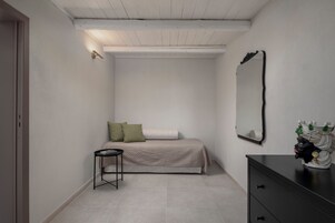 Quarto pequeno e bem organizado, com cama, mesinha, cômoda e espelho.