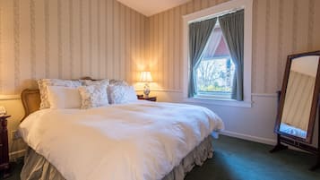 Cama bem arrumada com cabeceira estampada em flor, luminária de cabeceira e janela com cortinas.