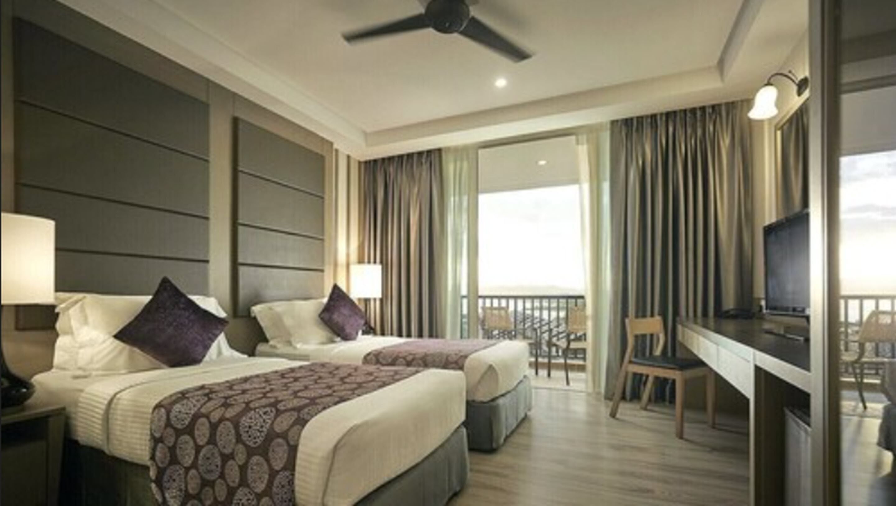Quarto de hotel com duas camas, uma escrivaninha, uma cadeira e uma varanda com cortinas.