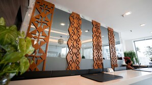 Uma área de recepção com design moderno, com balcão de atendimento, painéis decorativos de madeira e uma grande janela que oferece iluminação natural.