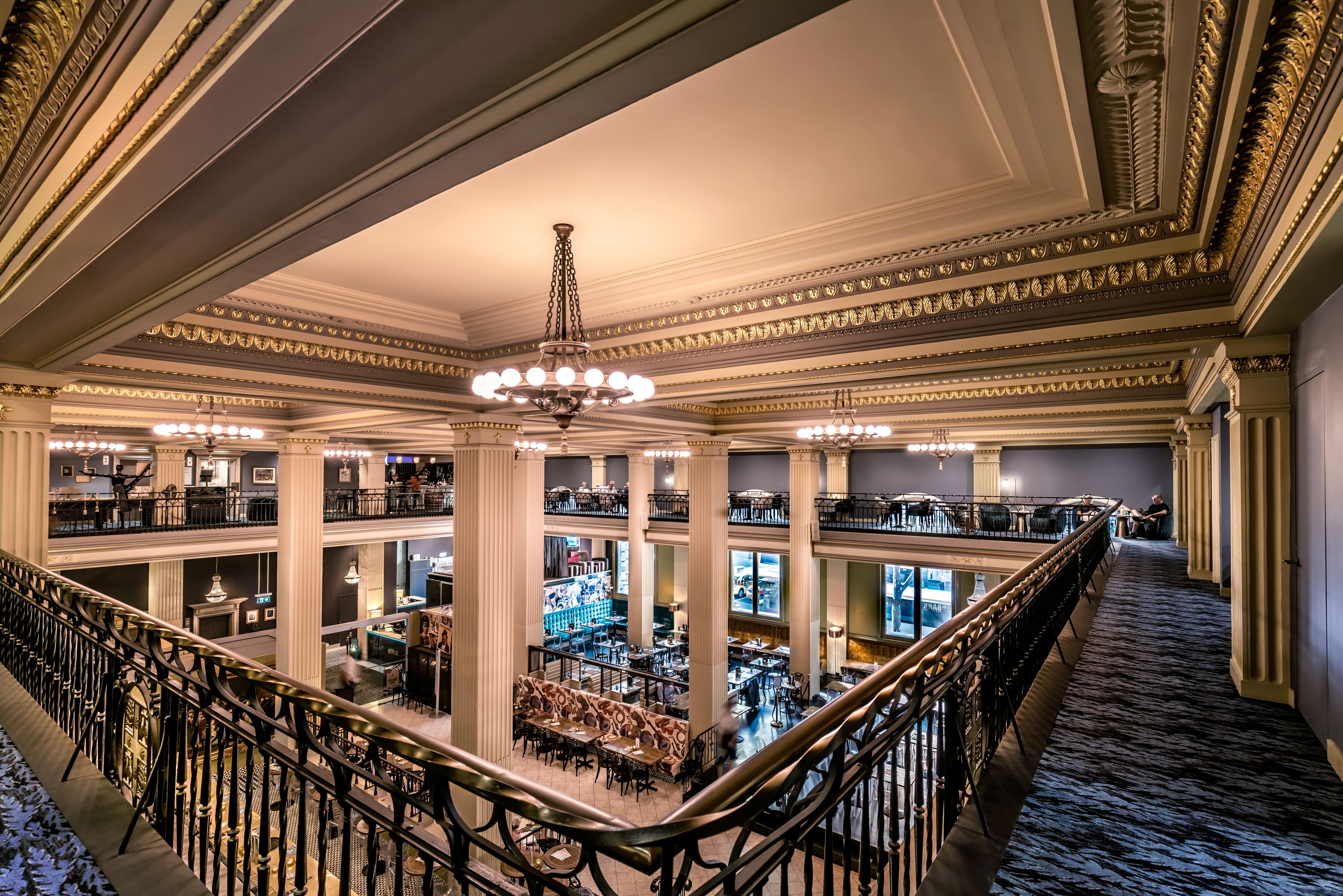 Um hall imponente com teto alto, colunas decoradas e um lustre central.